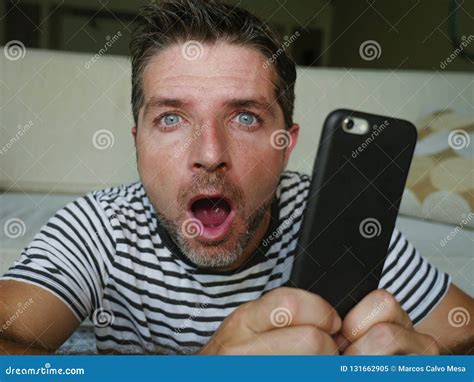 Young Perplexed And Shocked Man Using Mobile Phone Looking Internet