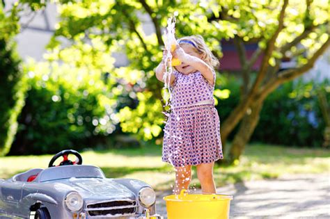 귀여운 화려한 유아 소녀는 여름 정원 야외에서 큰 오래된 장난감 자동차를 세탁합니다 비누와 물로 자동차를 청소하고 스폰지와 함께 놀고있는 행복한 건강한 어린 아이 귀여운에