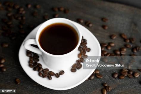 나무 테이블 배경에 구운 커피 콩커피 컵 나무 테이블에 흩어져 있는 커피 콩이 있는 검은 색 코프 잔 신선한 커피 콩 갈색에 대한 스톡 사진 및 기타 이미지 Istock