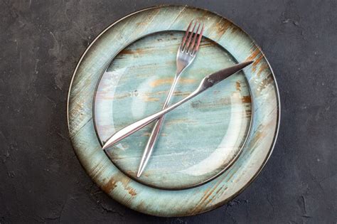 Вид сверху синяя тарелка с вилкой и ножом внутри на темной поверхности ...