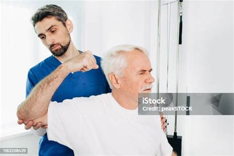 그는 자신의 큐빗을 스트레칭하는 동안 수석 환자를 들고 남성 물리 치료사 웰빙 센터에서 물리 재활 성인에 대한 스톡 사진 및 기타 이미지 Istock
