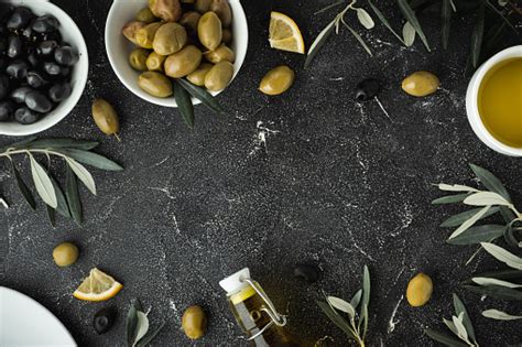 녹색과 검은 색 올리브는 올리브 오일이 든 병 옆에 흰색 그릇에 담겨 있으며 검은 색 배경에 나뭇잎 냉간 압착 오일 한 병