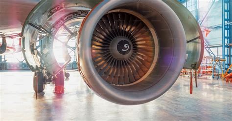 게이트 외부에 밝은 빛이 있는 항공 격납고에서 수리를 위해 열린 후드가 있는 비행기 엔진의 산업 보기 사진 Unsplash의