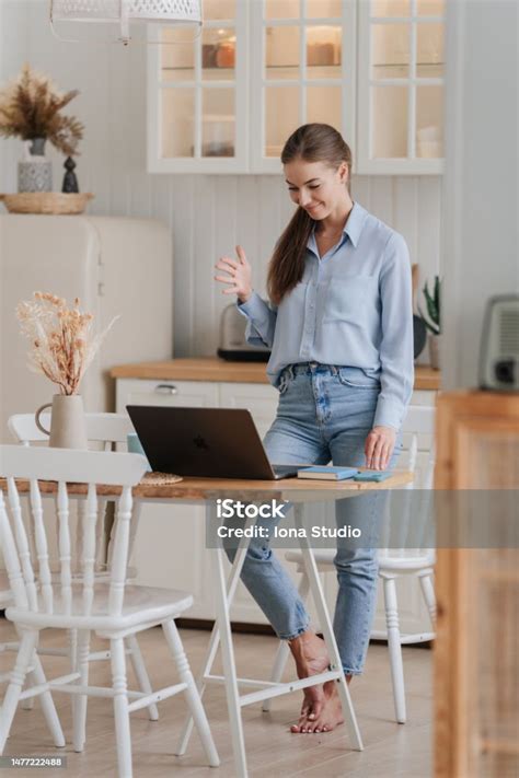 청바지와 셔츠를 입은 성공적인 어린 학생 소녀는 부모와 인터넷을 통해 노트북으로 부엌 테이블에 서 있습니다 캐주얼의 쾌활한 여성은 주말을 즐긴다 국내 레저 화상 회의에 대한