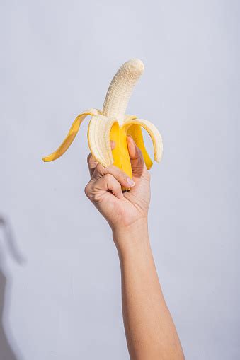 깨끗한 흰색 배경에 부분적으로 껍질을 벗긴 잘 익은 바나나를 들고 있는 손은 부드러운 노란색 과육 열대의 신선함 및 건강한 달콤한 과일의 자연스러운 질감을 보여줍니다 개념에