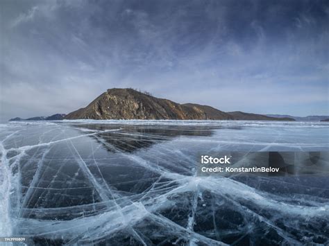 눈과 호 아 르 서 리로 덮인 돌이 있는 얼어 붙은 섬 근처의 바이칼 호수의 균열과 균열이 있는 투명 한 얼음 부드러운 미 끄 러운 표면은 구름과 하늘 아래 반사와 유리