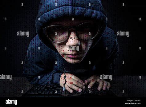 Binary Code On The Background Of A Hacker In A Hood And Glasses Sits At The Keyboard And Looks
