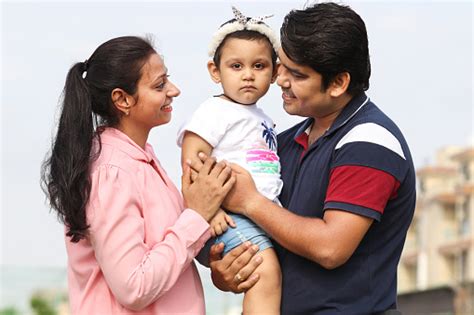 공원이나 정원에 함께 시간을 보내는 귀여운 사랑스러운 딸과 함께 행복한 젊은 인도 부모의 초상화 웃고 있는 아버지와 어머니는 여자 아이를 안고 그녀를 바라보고 있다 2 3