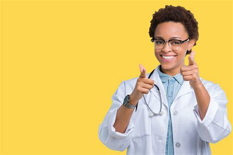 젊은 아프리카계 미국인 의사 여자 행복 하 고 재미 있는 얼굴로 카메라를 손가락을 가리키는 격리 된 배경 위에 의료 코트를 입고 좋은 에너지와 느낌입니다 가리키기에 대한
