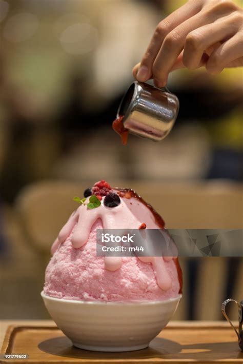 婦女手倒草莓糖漿在 Kakigori 的根日元草莓或草莓韓國剃須冰 Patbingsu 或 Bingsu 冷凍甜點在咖啡館的木桌上 照片檔及更多 士多啤梨 照片 Istock