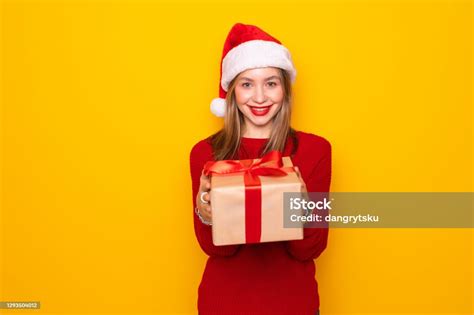 가슴 가까이에 선물 상자를 들고 꽤 기뻐하는 여자는 니트 점퍼와 산타 모자 고립 된 노란색 배경을 착용 겨울에 대한 스톡 사진 및 기타 이미지 Istock