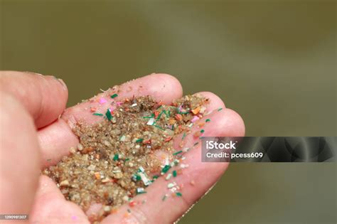 손의 클로즈업 사이드 샷은 해변 모래로 오염 된 미세 플라스틱 폐기물을 보여줍니다 미세 플라스틱은 바다에서 오염됩니다 수질 오염과 지구 온난화의 개념 Microplastic