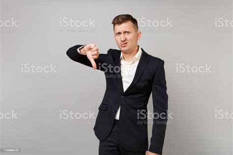 아래로 클래식 블랙 정장 흰색 셔츠 보여주는 엄지손가락에 혐오 젊은 사업가 Bewildered 스튜디오에서 회색 벽 배경에 고립 성과 경력 부 비즈니스 개념입니다 복사