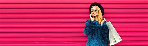 파란색 모피 코트를 입은 스마트 폰 분홍색 배경에 검은 둥근 모자 광고 텍스트를위한 빈 복사 공간을 부르는 쇼핑백을 가진 세련된