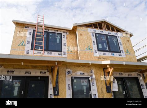 New Homes Under Construction With Scaffolding And Plywood Walls Workers On Site Building In