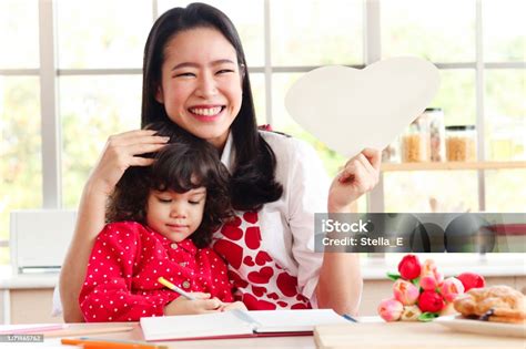 엄마의 무릎에 앉아 어린 아이 딸 소녀 메시지는 빈 하트 모양의 종이를 들고 행복 미소 아름다운 젊은 아시아 엄마 동안 어머니의 날을 축하하기 위해 수제 카드를 준비 아이