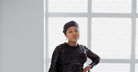 검은 이브닝 웨어와 모자를 쓴 세련된 아프리카 이슬람계 미국인 여성이 흰색 배경 위에 포즈를 취하면서 카메라를 보고 있다 아름다움 패션 및 우아함의 개념 사진