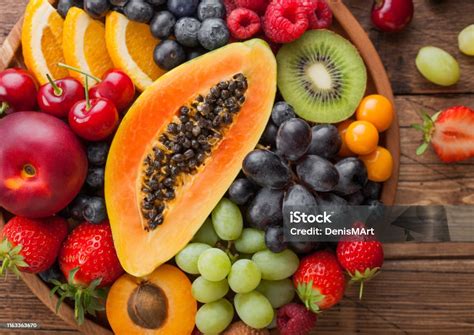 나무 부엌 배경에 둥근 나무 접시에 신선한 원시 유기농 여름 열매와 이국적인 과일 파파야 포도 넥타린 오렌지 라즈베리 키위 딸기 열매 체리 매크로 0명에 대한 스톡 사진 및