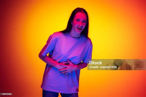 젊은 매력적인 소녀의 절반 길이 초상화 네온 라이트 필터에서 오렌지색 배경에 고립 된 포즈를 취하는 긴 머리카락을 가진 학생