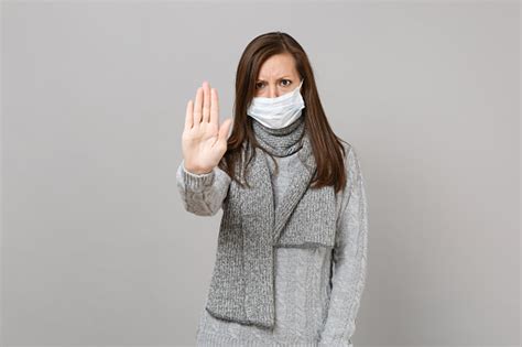 스웨터 젊은 여자는 회색 배경에 고립 손바닥 중지 제스처를 보여주는 메 마른 얼굴 마스크 스카프 건강 한 라이프 스타일 아픈