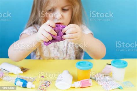 금발의 소녀는 파란색 배경에 고립 된 보라색 점액을 보유하고 있습니다 점액 장난감을 가지고 노는 아이 점액 만들기 공간을