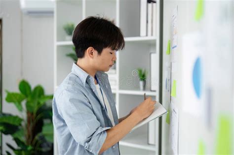 Young Business Analyst Taking Notes While Reviewing Data Charts In A