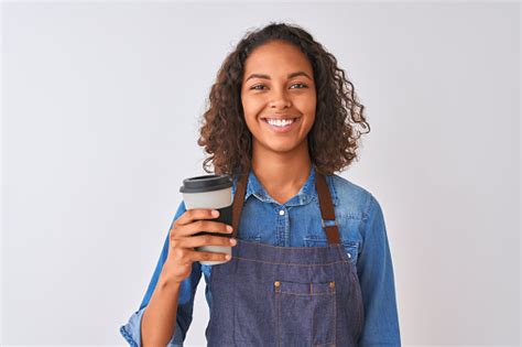 젊은 브라질 바리스타 여자 마시는 치아를 보여주는 자신감 미소와 함께 행복한 얼굴 서서 미소와 고립 된 회색 배경을 통해 커피를 빼앗아 바리스타에 대한 스톡 사진 및 기타