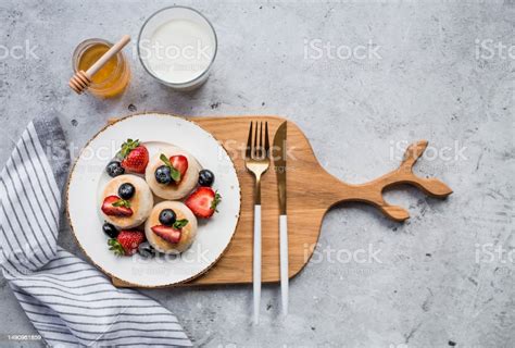 코티지 치즈 팬케이크 신선한 블루베리 딸기 꿀 민트 잎을 곁들인 러시아 치즈 케이크가 회색 콘크리트 테이블 위의 세련된 나무