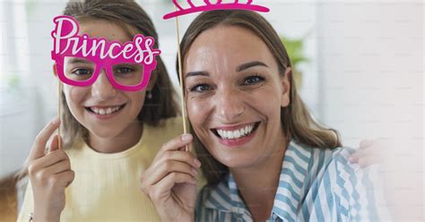 밝은 벽의 배경에 재미 있는 가족 어머니와 그녀의 딸 소녀가 종이 액세서리를 가지고 있다 엄마와 아이는 막대기에 종이 왕관을 들고 있습니다 사진 Unsplash의