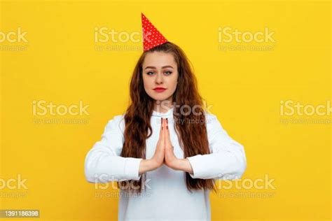 축하 모자에 친절한 젊은 귀여운 여자 기도 또는 Namaste 제스처에 손을 잡고 노란색 배경의 화려한 스튜디오 초상화 휴일과 파티 개념 20 24세에 대한 스톡 사진 및