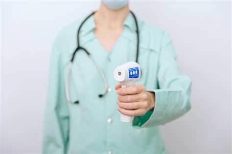 의사의 손에 온도 측정 총 적외선 등자극 온도계 총을 사용하여 바이러스 증상에 대한 체온을 확인할 준비가 된 보호 수술 용 마스크를 착용한 의사의 클로즈업 샷 19에 대한