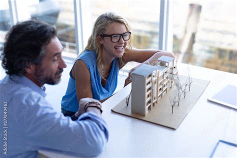 Male And Female Architect Discussing Over Architectural Model At Table In A Modern Office Stock
