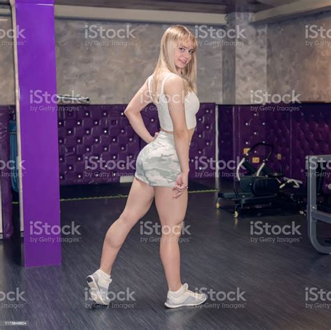 아름 다운 피트 니스 행복 금발 소녀 스포츠 착용 에 완벽 한 몸 체육관에서 포즈와 미소 젊은 선수 미소와 그녀의 근육을