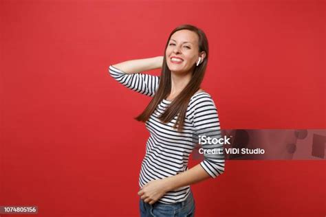 무선 이어폰 밝은 빨간 벽 배경에 고립 된 음악 듣기와 캐주얼 스트라이프 옷에서 웃는 젊은 여자의 초상화 사람들이 진심으 감정 라이프 스타일 개념 복사 공간을 비웃는 다