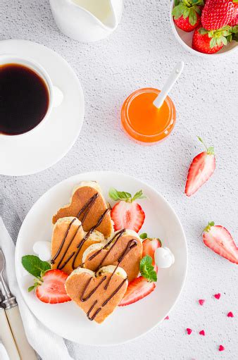 하트 모양의 팬케이크와 초콜릿 소스 신선한 딸기를 하얀 접시에 얹고 커피 한 잔을 곁들인 밝은 배경에 놓습니다 발렌타인 데이