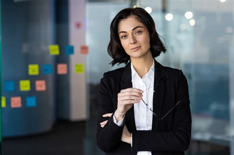 배경에 스티커 메모가 있는 현대적인 사무실 환경에서 자신감 넘치는 사업가 안경을 들고 정장 정장을 입고 회의 준비 확신을 가지고 카메라를 보고 있습니다 개념에 대한 스톡