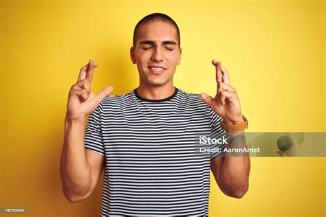 노란색 고립 된 배경 제스처 손가락 위에 줄무늬 티셔츠를 입고 젊은 잘 생긴 남자는 희망과 눈을 감고 미소 교차 행운과 미신 개념 T 셔츠에 대한 스톡 사진 및 기타 이미지