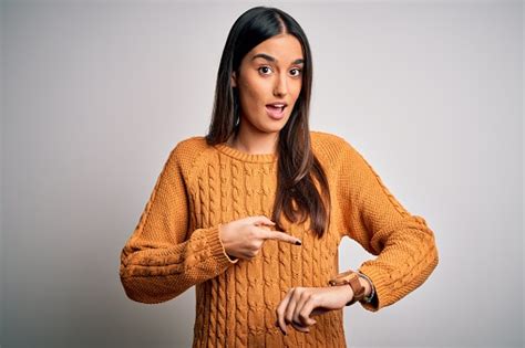 젊은 아름다운 갈색 머리 여자 를 입고 캐주얼 스웨터 위에 고립 된 흰색 배경 에 서둘러 가리키는 시계 시간 조바심 화가 와 화가 마감 지연 가리키기에 대한 스톡 사진 및