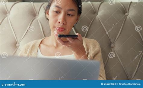 Close Up Asian Girl With Laptop On Bed Use Smartphone Giving Voice Commands To Virtual Assistant
