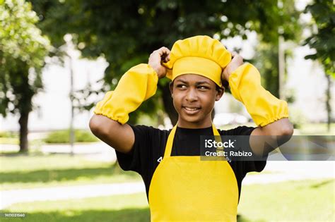 흑인 아프리카 십대는 요리사 모자와 노란 앞치마 유니폼을 입고 요리사 모자를 만집니다 카페 또는 레스토랑을위한 창조적 인 광고 12 13세에 대한 스톡 사진 및 기타 이미지