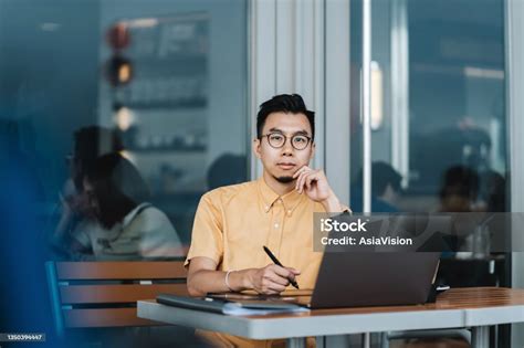 카페에서 야외에 앉아있는 동안 펜으로 그림을 그리는 디지털 그래픽 태블릿에서 일하는 자신감 있는 젊은 아시아 남성 디자이너의