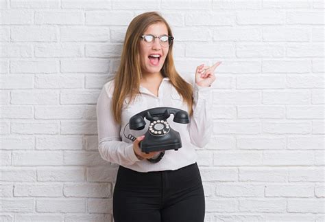 매우 행복 한 측에 손 및 손가락으로 가리키는 빈티지 전화를 들고 흰 벽돌 벽을 통해 젊은 성인 여자 가리키기에 대한 스톡 사진 및 기타 이미지 Istock