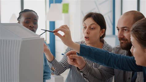 Close Up Of Workmates Analyzing Building Model And Maquette On Table To Design Construction