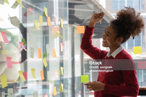 젊은 웃는 매력적인 사업가는 유리 벽에 스티커 메모를 사용하여 개발하고 성공으로 성장하기 위한 전략적 사업 계획을 작성합니다 가리키기에 대한 스톡 사진 및 기타 이미지