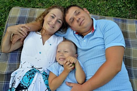 엄마 아빠와 작은 아들은 일몰 여름 날에 공원에서 잔디에 누워 꿈을 꾸고 있습니다 그들은 보고 미소를 지었다 초상화 위쪽에서 보기입니다 이미지의 가로 방향입니다 3 명에