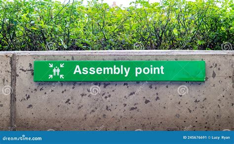Informative Green Assembly Point Sign With People Icon Graphic On Wall