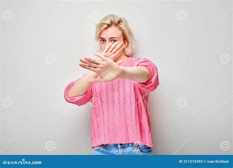 Blonde Woman In Pink Top Gesturing Stop With Her Hands Against A White
