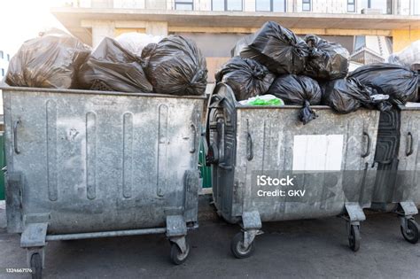 많은 큰 금속 과부하 쓰레기통 의 행은 도시 시내 또는 교외 지역의 주거 건물 근처 검은 플라스틱 쓰레기 쓰레기 봉투로 가득 합니다 재활용 불가능한 선별 쓰레기 수집 0명에