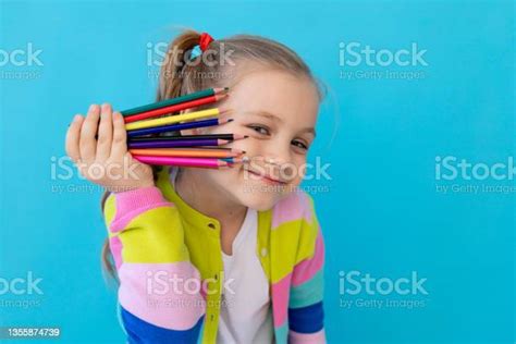 줄무늬 재킷에 색깔의 연필을 가진 귀여운 어린 소녀의 초상화 교육과 드로잉의 개념 사진 스튜디오 파란색 배경 텍스트 장소 연필에