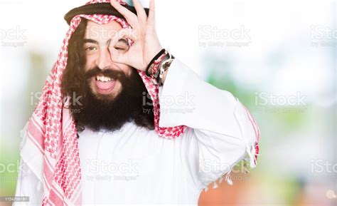 전통적인 서구인을 입고 긴 머리를 가진 아라비아 사업가 손 미소와 제스처를 확인 하 고 스카프 행복 한 얼굴로 손가락을 통해 보는 눈 구멍에 대한 스톡 사진 및 기타 이미지